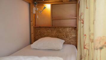 Uma cama de solteiro com cabeceira de madeira e travesseiro branco em um quarto estilo cabana, com vigas de madeira aparentes e teto inclinado.