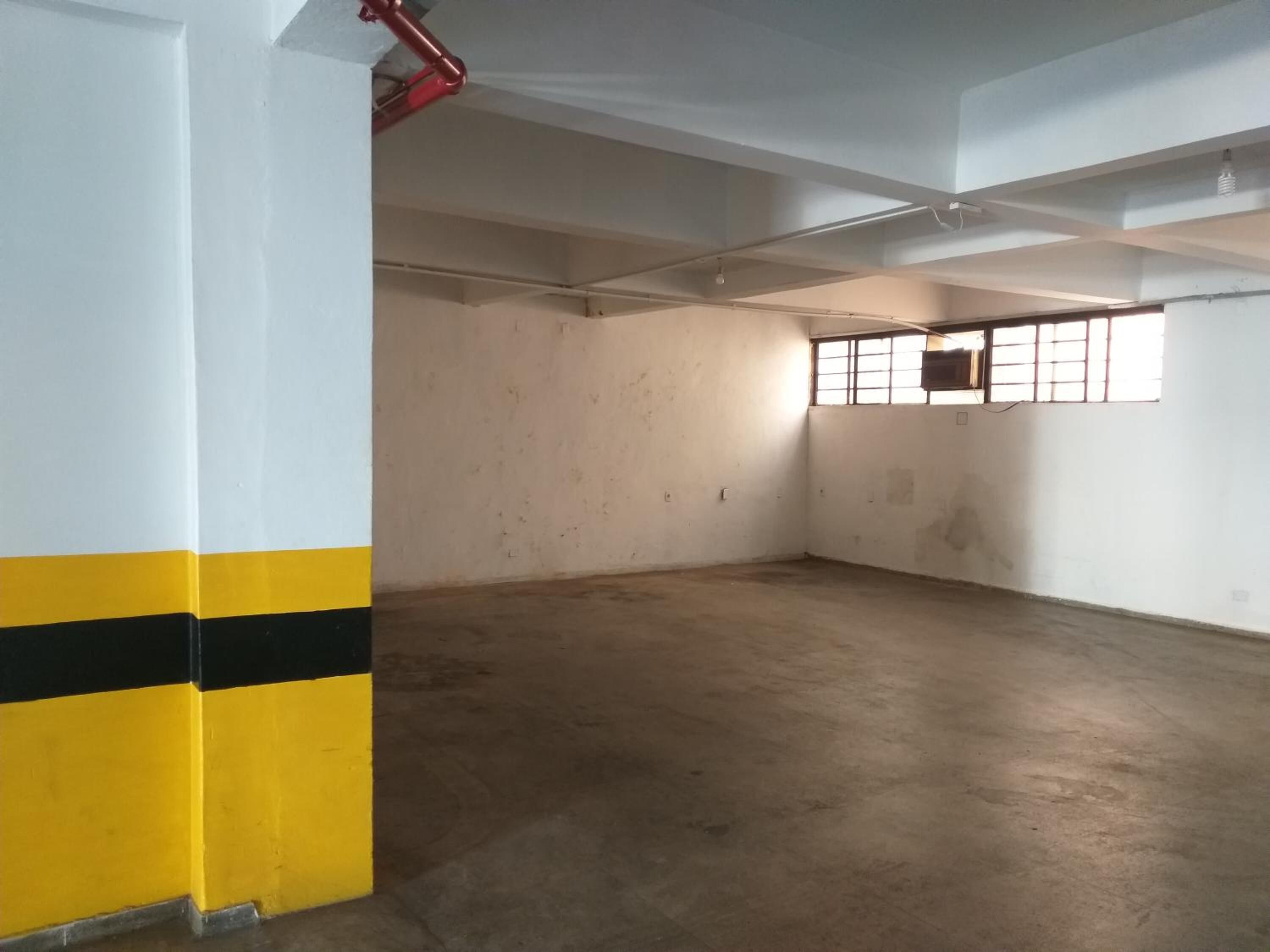 Um espaço amplo e vazio, com piso de concreto e paredes brancas.