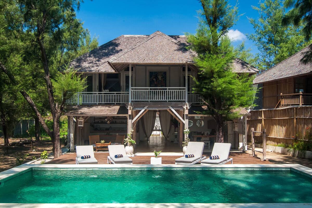 Uma casa de dois andares com piscina, cadeiras de descanso e um deque de madeira.