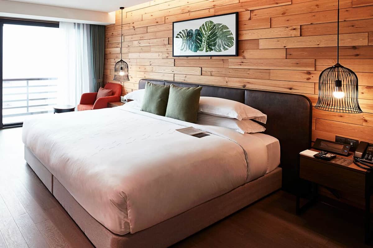 Quarto de hotel moderno com uma cama grande, uma escrivaninha, uma cadeira e vista para o exterior.
