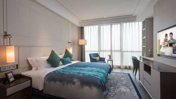 Quarto de hotel moderno com uma cama grande, uma escrivaninha, uma cadeira e uma televisão.