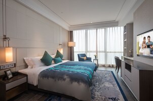 Quarto de hotel moderno com uma cama grande, uma escrivaninha, uma cadeira e uma televisão.