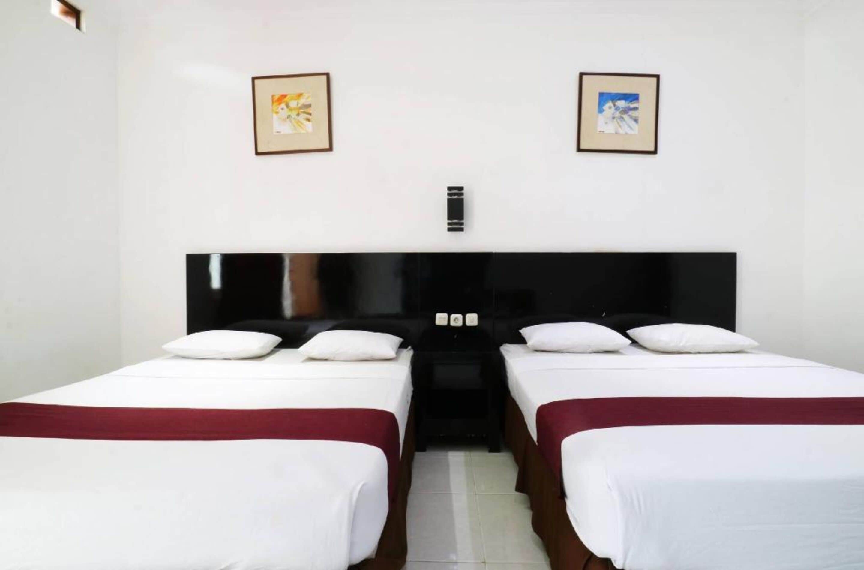 Quarto de hotel com duas camas de solteiro, um espelho grande sobre a cabeceira e dois quadros na parede.