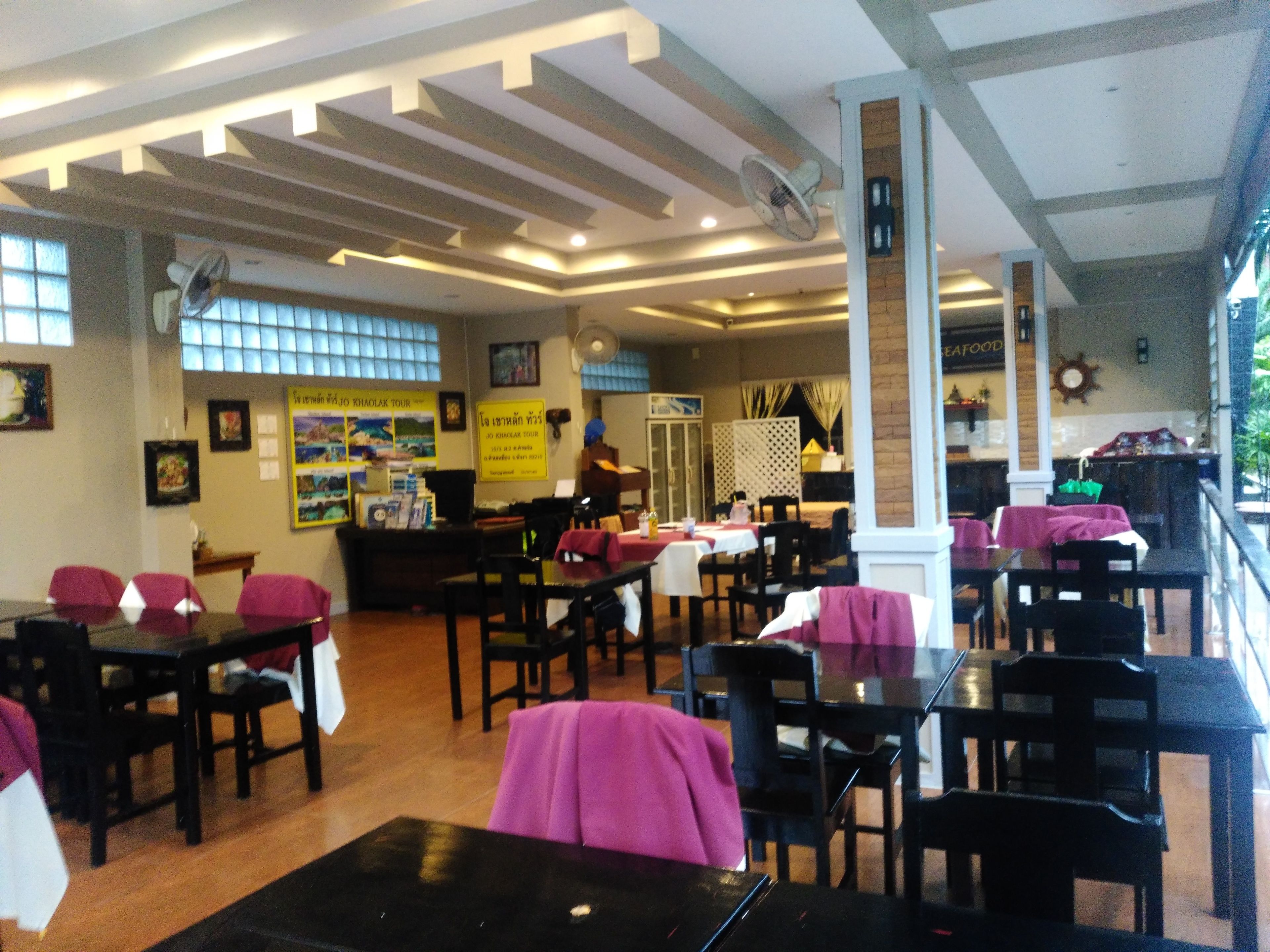 Um restaurante com várias mesas e cadeiras, um ventilador de teto e uma placa na parede.