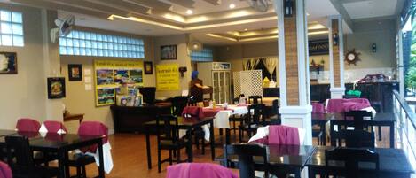 Um restaurante com várias mesas e cadeiras, um ventilador de teto e uma placa na parede.