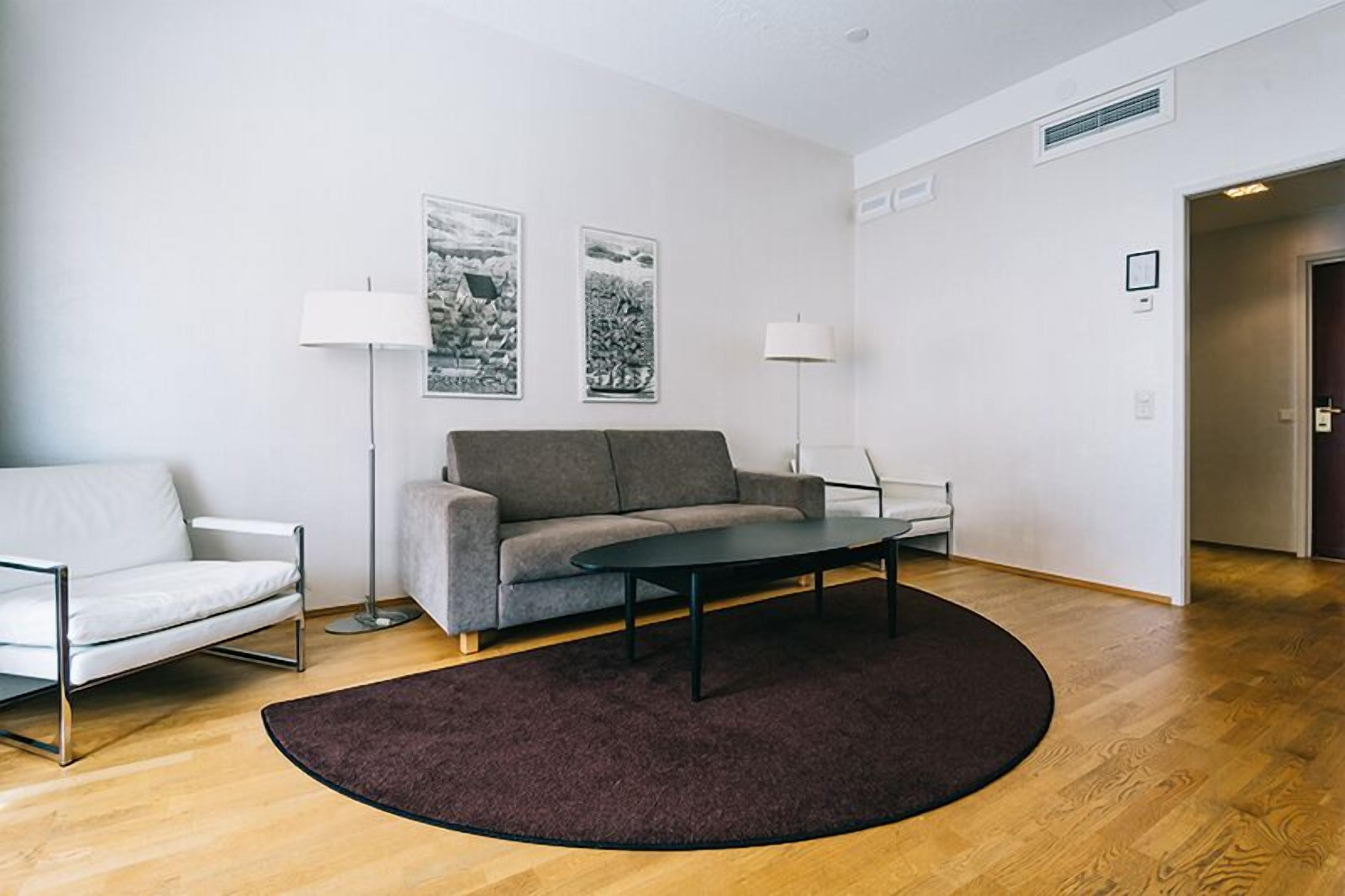 Uma sala de estar moderna com um sofá cinzento, uma poltrona branca, uma mesa de centro redonda e duas luminárias de chão.