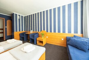 Quarto de hotel com duas camas, um sofá, uma mesinha e uma cadeira.