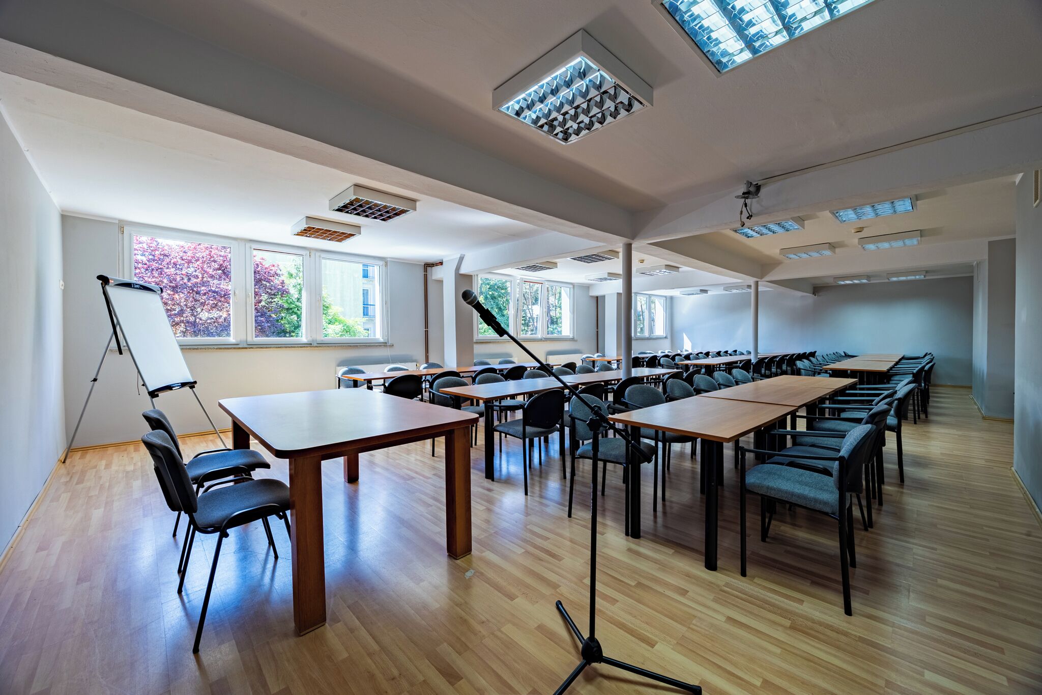 Sala de conferência com várias mesas e cadeiras, janelas amplas e um quadro branco.