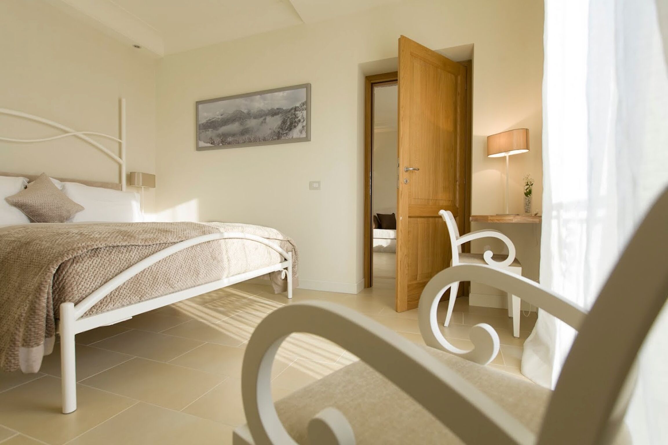 Um quarto com uma cama, uma cadeira, uma porta de madeira e um quadro na parede.