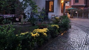 Um edifício de dois andares com telhado inclinado, janela visível e um jardim com flores amarelas.