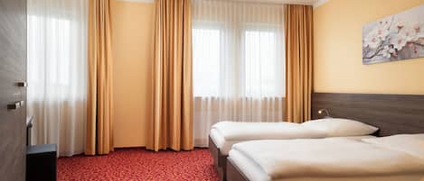 Quarto de hotel com duas camas, um tapete vermelho estampado, cortinas bege e um quadro na parede.