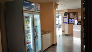 Um corredor com uma geladeira Panasonic abastecida com bebidas, um freezer compacto e um balcão de madeira com um quadro de menu.