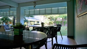 Um restaurante com mesa de vidro, cadeiras pretas e vista para um jardim.
