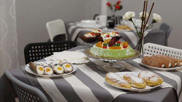 Uma mesa de jantar com diversos doces e pastéis, incluindo um bolo verde com frutas e um prato de pastéis recheados com creme.