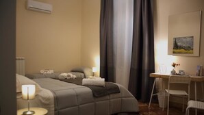 Quarto de hotel com uma cama, uma escrivaninha com cadeira, uma luminária e um quadro na parede.