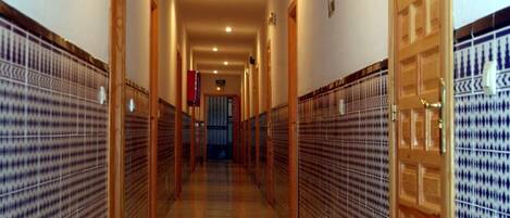 Corredor de hotel com paredes azulejadas, portas de madeira e chão em azulejo.