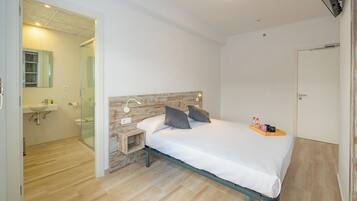 Quarto com cabeceira de madeira, mesa de cabeceira, cama com roupa de cama branca e um pequeno suporte com objetos.