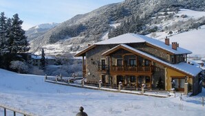 Um chalé com varanda, rodeado por montanhas e árvores cobertas de neve.