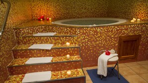 Uma área de spa com piso de azulejos, banheira de hidromassagem, degraus com toalhas e um armário de madeira.