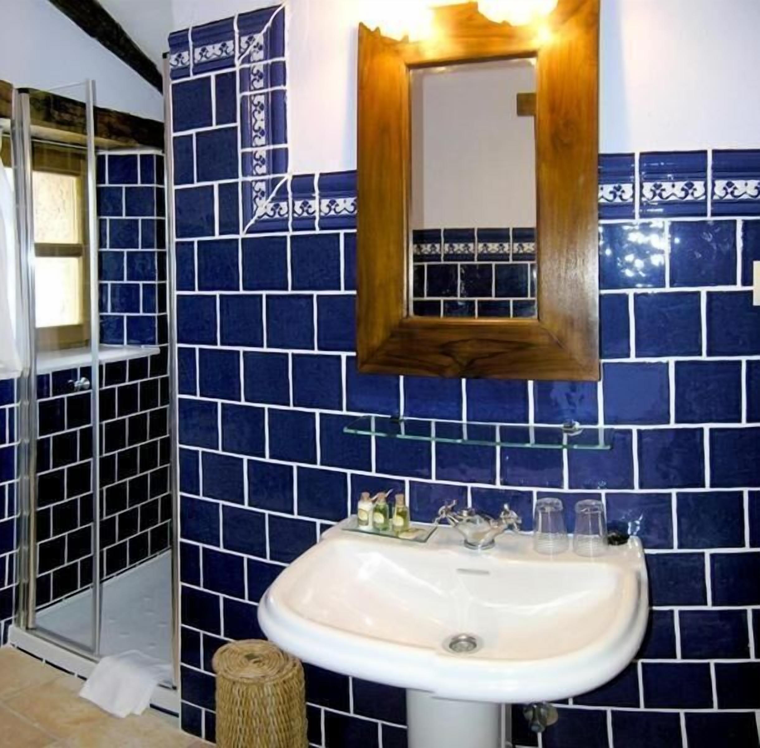 Casa de banho com lavatório, espelho e paredes azulejadas em azul.