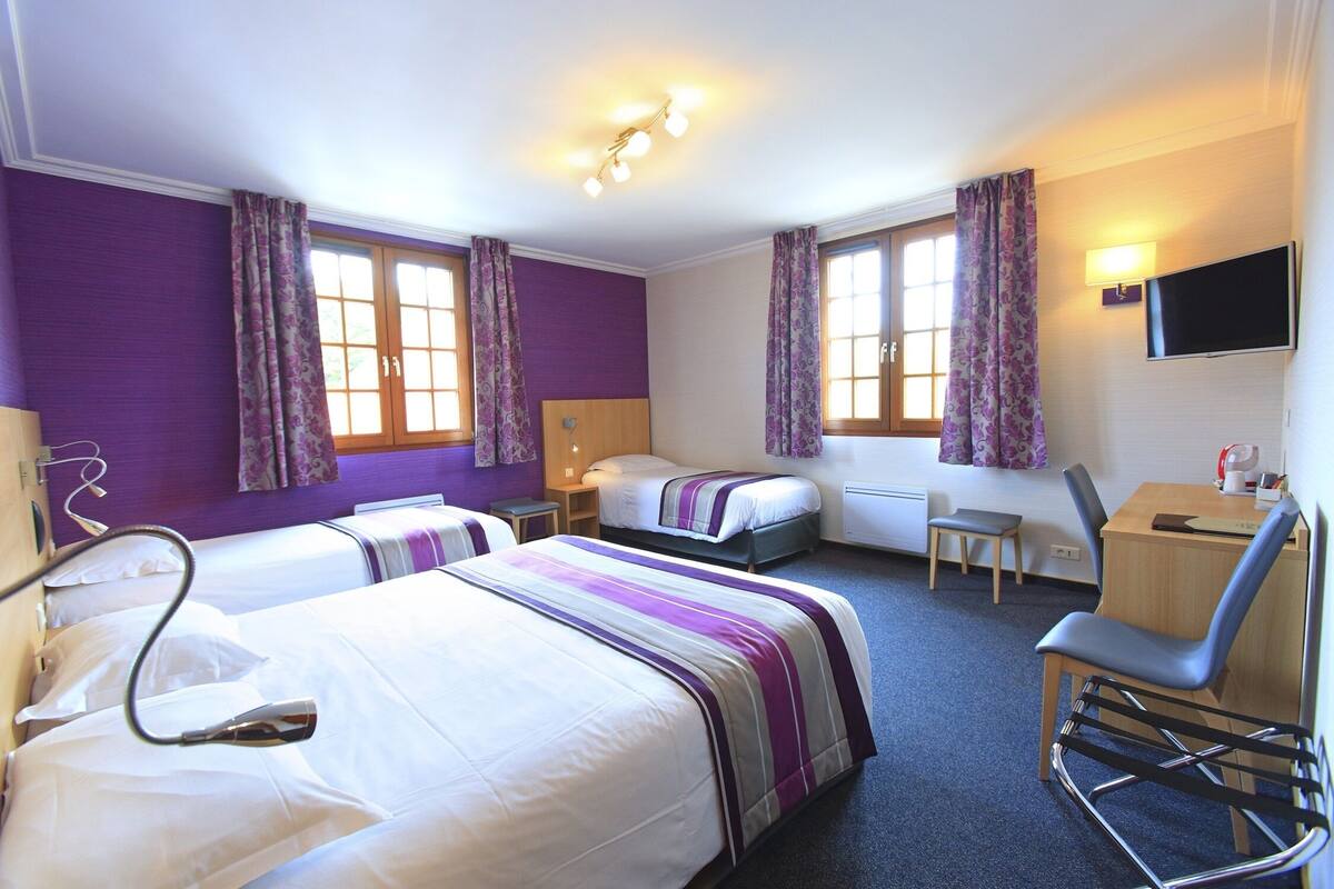Quarto de hotel com duas camas, uma escrivaninha, uma cadeira e uma televisão.
