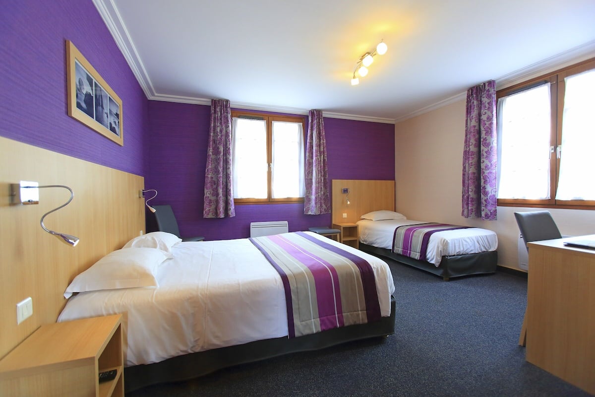 Quarto de hotel com duas camas, uma escrivaninha e uma cadeira.