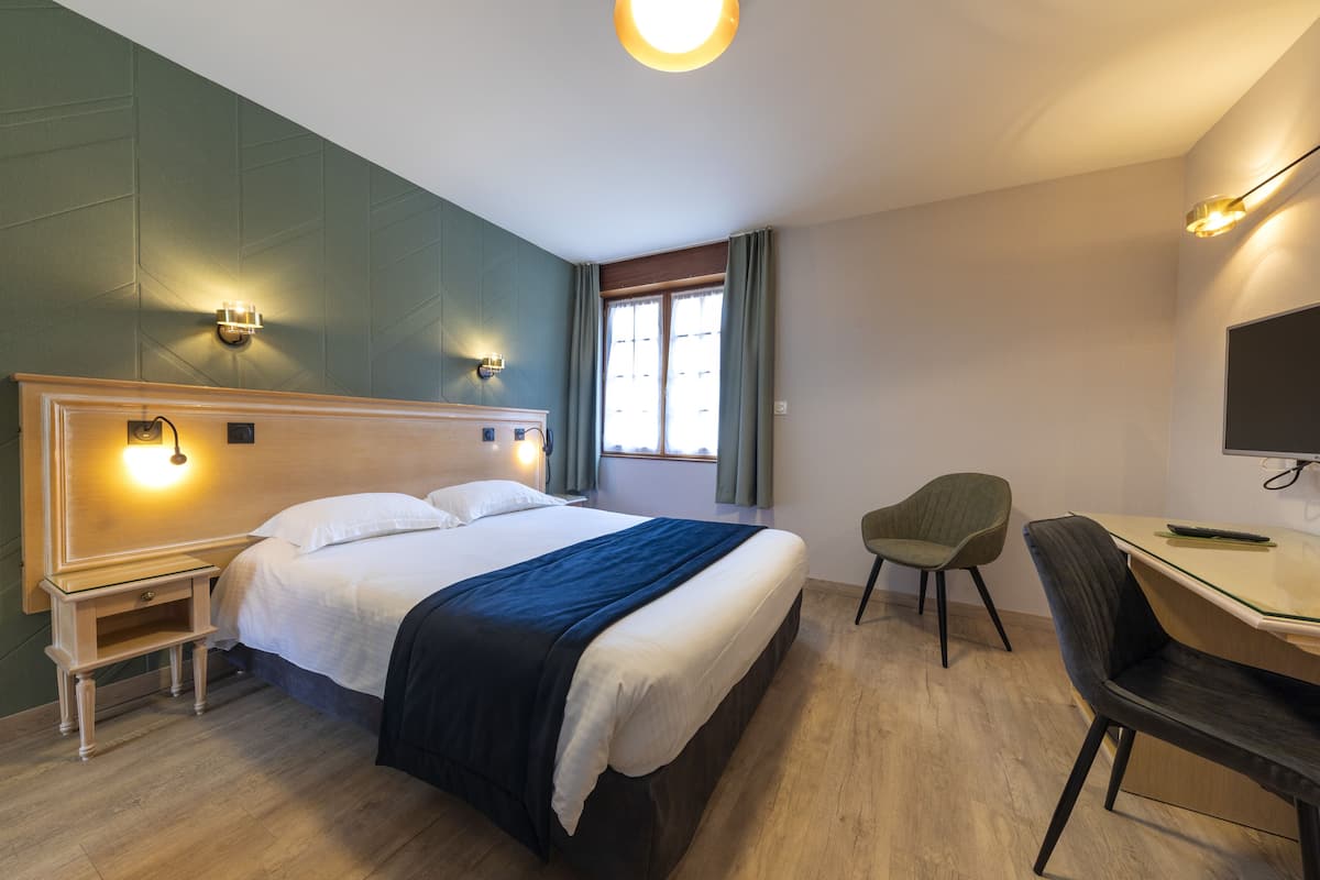 Quarto de hotel com cama, mesa de cabeceira, escrivaninha e cadeira.