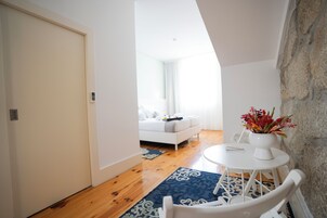 Uma sala de estar moderna com um sofá branco, uma mesa redonda branca e um vaso de flores, além de um tapete azul estampado.