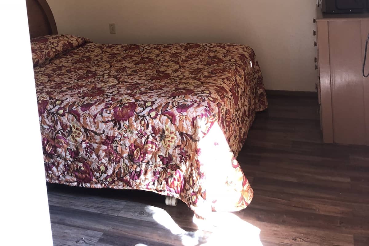 Quarto com cama, ventilador de teto, pequena janela com vista e armário.