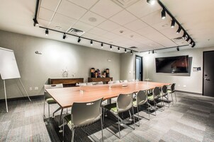 Sala de conferência com uma longa mesa, cadeiras, um quadro branco e uma tela de televisão na parede.