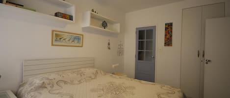 Quarto com cama, guarda-roupa, porta e prateleiras com objetos.
