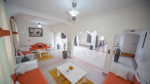 Um saguão de hotel com sofás laranja, uma mesa de centro branca e um lustre.