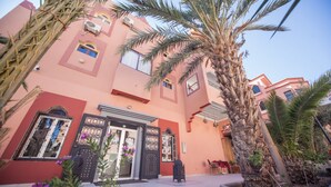 Um hotel com fachada rosa, grandes janelas e uma palmeira em primeiro plano.