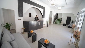 Uma área de recepção de hotel com design moderno, incluindo um balcão de recepção, uma escadaria e um espaço de estar com um sofá e uma mesa com laranjas.