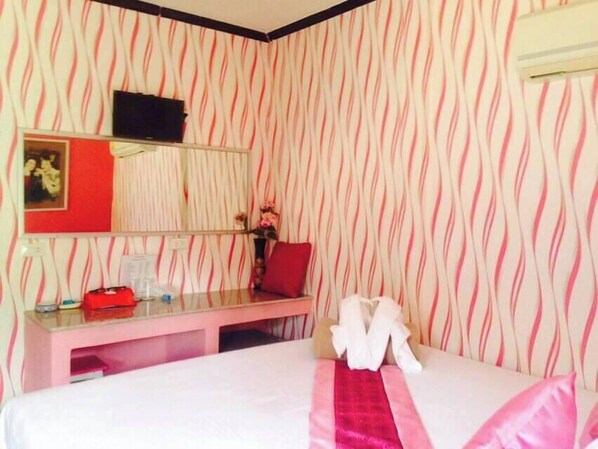Quarto de hotel com cama, escrivaninha, espelho e almofada vermelha.