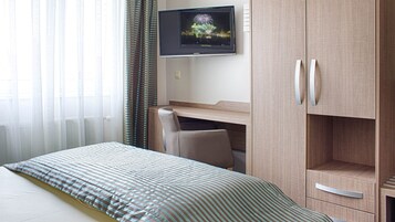 Quarto de hotel com cama, mesa com cadeira, televisão e guarda-roupa.
