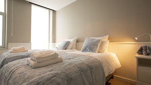 Quarto moderno com duas camas, uma mesa de cabeceira e um criado-mudo.