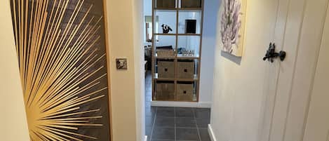 Um corredor com uma porta decorativa, piso ladrilhado, parede branca com um quadro e outra porta branca no final.