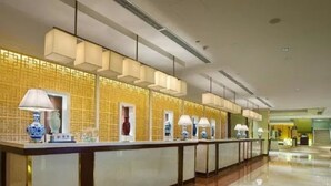 Uma área de recepção de hotel com um balcão comprido, várias luminárias e um papel de parede estampado.