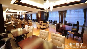 Uma sala de café amplo com várias áreas de estar, incluindo mesas e cadeiras, e grandes janelas que proporcionam luz natural.
