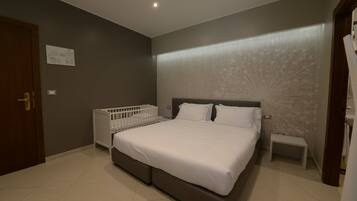 Quarto com cama grande, berço, mesa de cabeceira pequena e uma porta.