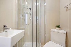 Uma casa de banho moderna com cabine de duche em vidro, lavatório branco e sanita.