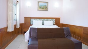 Quarto com cama, mesa de cabeceira, cabeceira de madeira, janela com cortinas e ar condicionado fixado na parede.