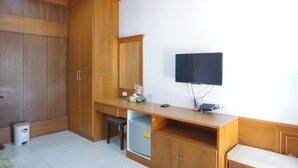 Quarto compacto com escrivaninha de madeira, televisão, mini-frigorífico e guarda-roupa.