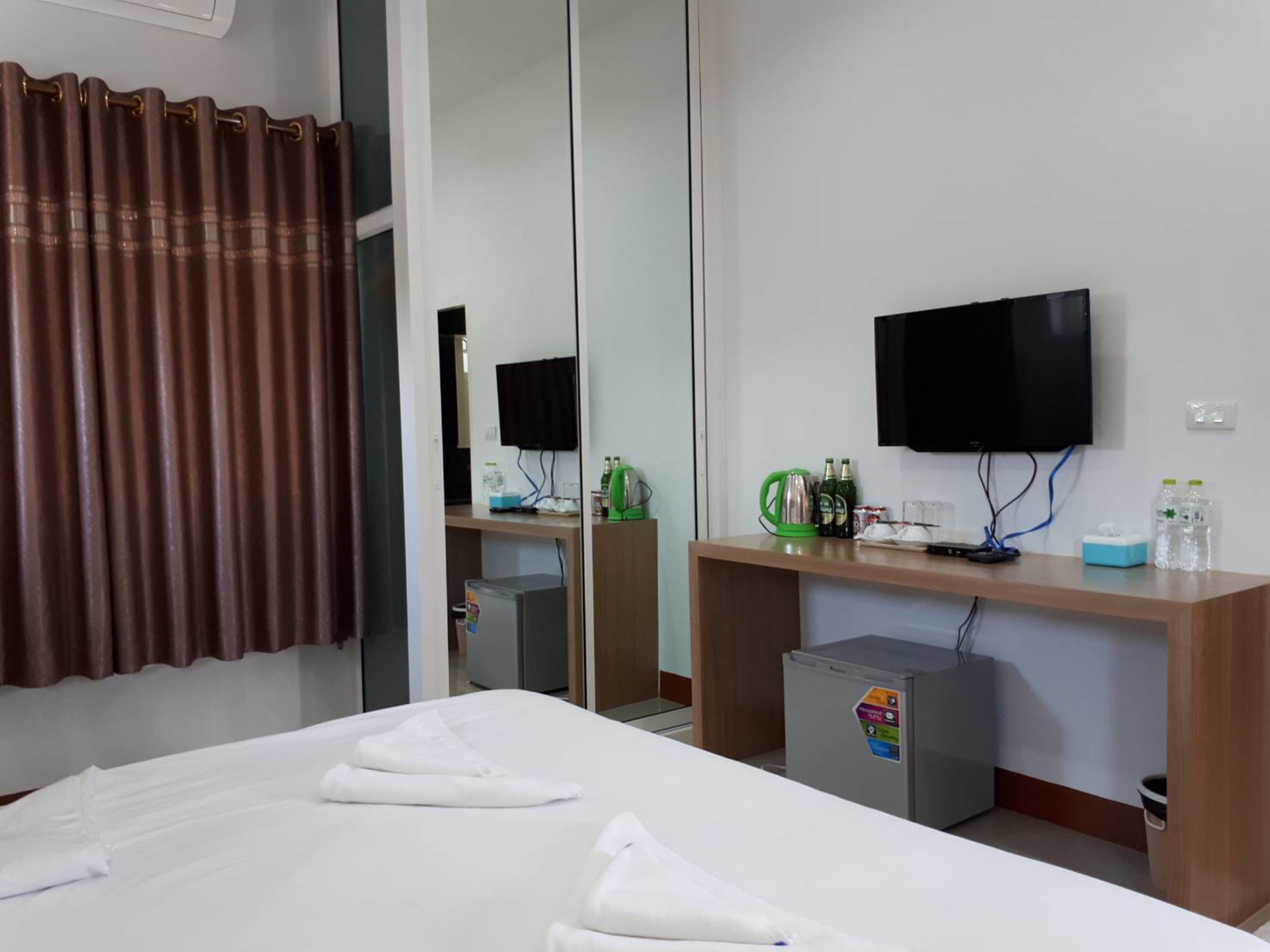 Quarto de hotel com cama, escrivaninha com televisão, espelho e pequeno frigorífico.
