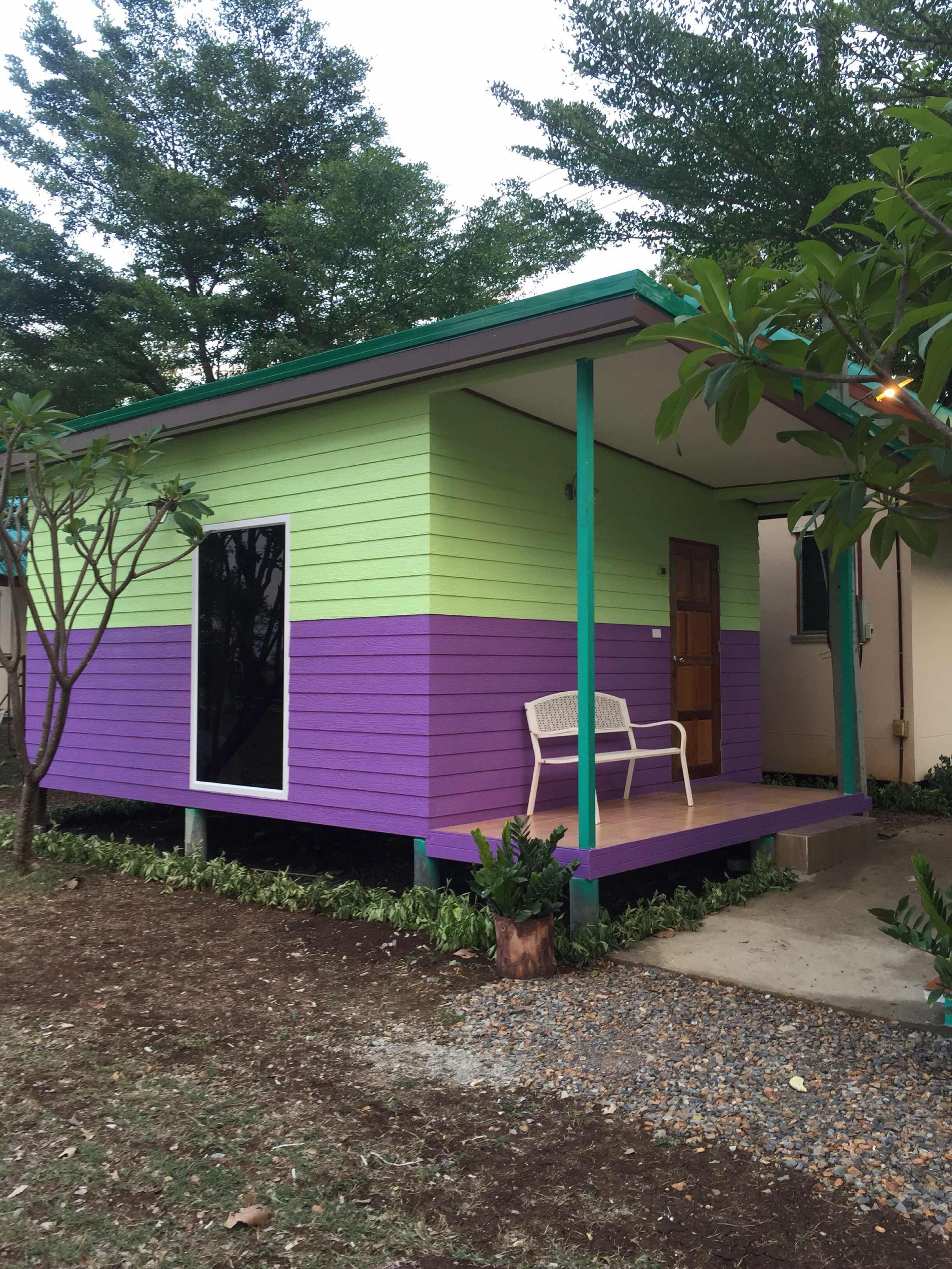 Uma casa pequena, térrea, com varanda e um banco.