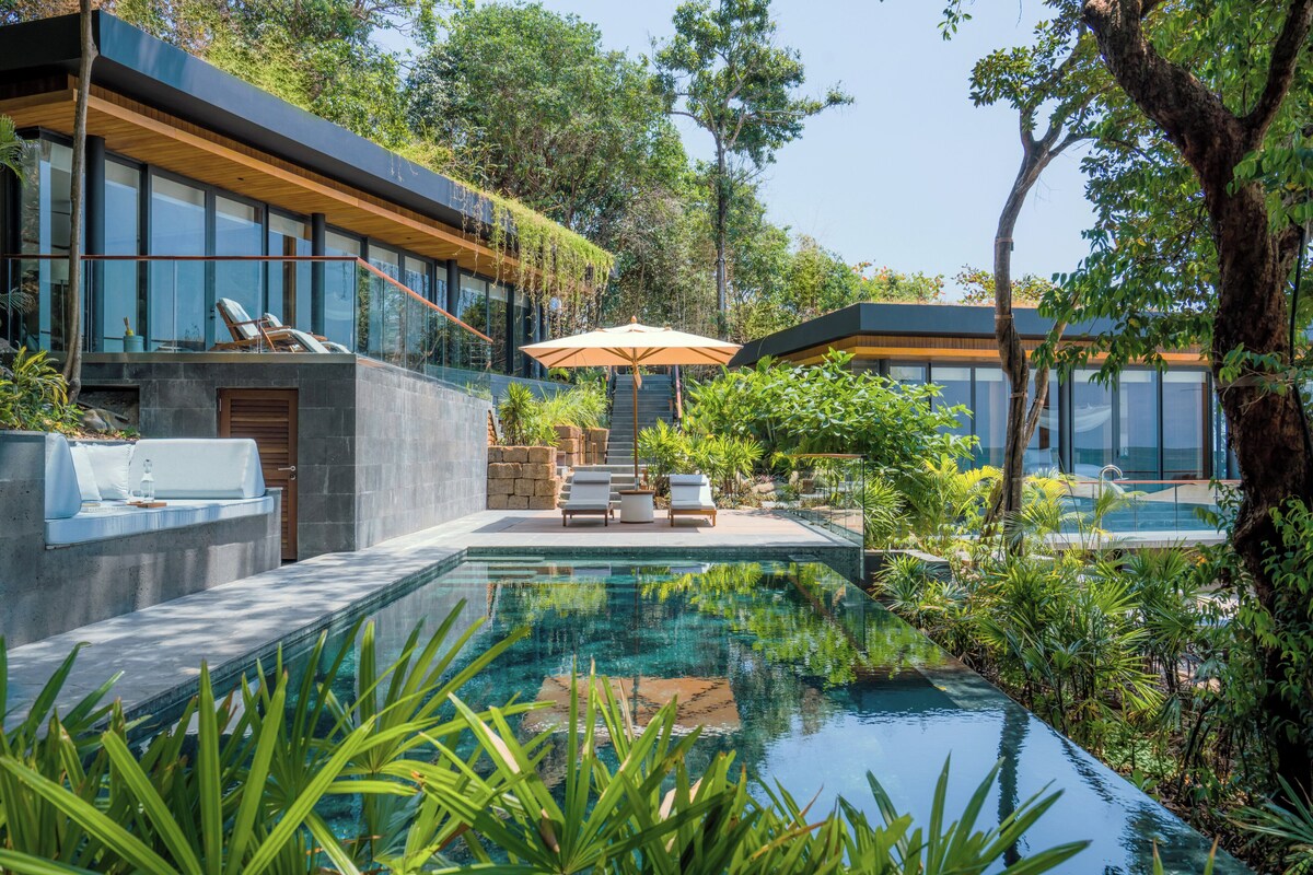 Área de piscina moderna ao ar livre, com espreguiçadeiras e um grande guarda-sol.