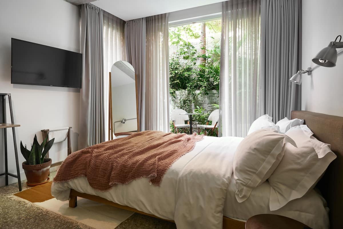 Quarto com cama, televisão, planta em vaso e vista para um jardim pela janela.