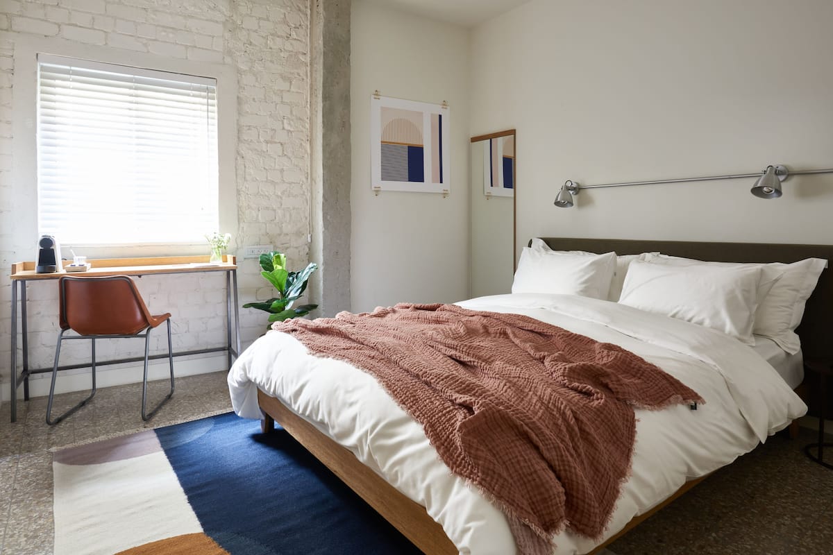 Quarto com cama, escrivaninha, cadeira e janela com persianas.