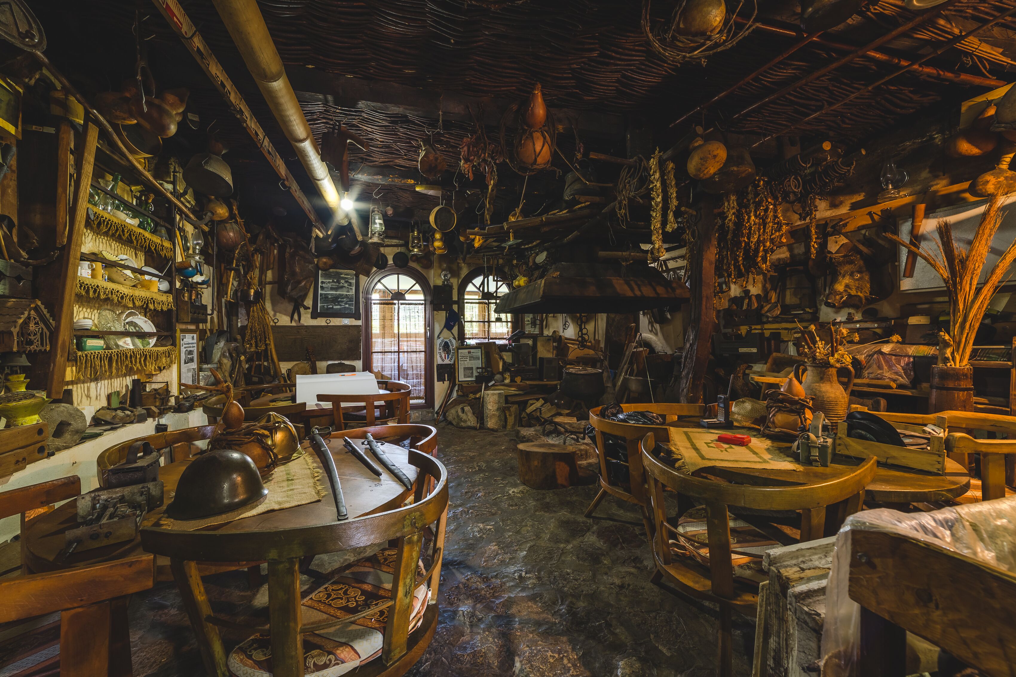 Um interior rústico com mobiliário de madeira, piso de pedra, utensílios de cozinha e diversos objetos decorativos.